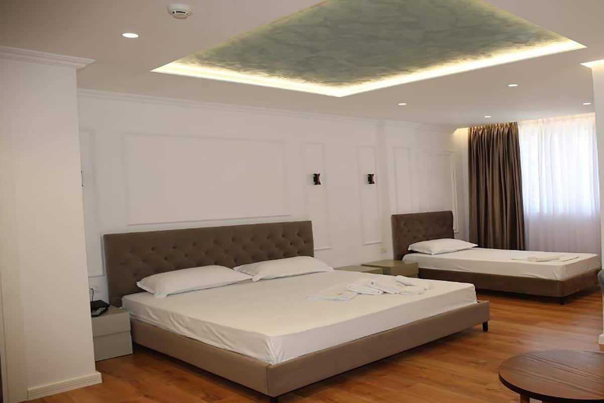 Quarto de hotel com duas camas, uma escrivaninha de madeira e uma mesa redonda.
