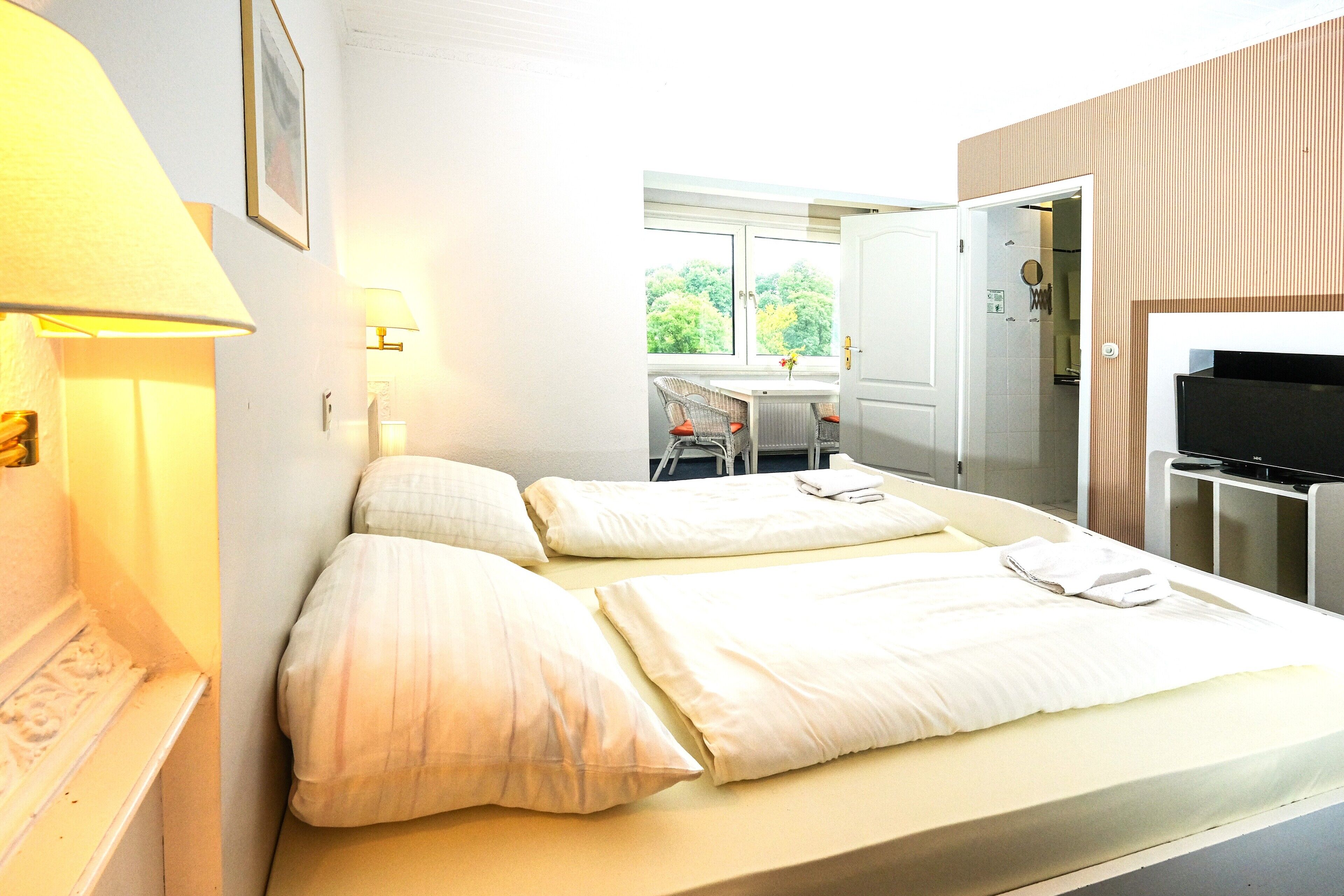 Quarto de hotel com cama, abajures, escrivaninha e televisão.