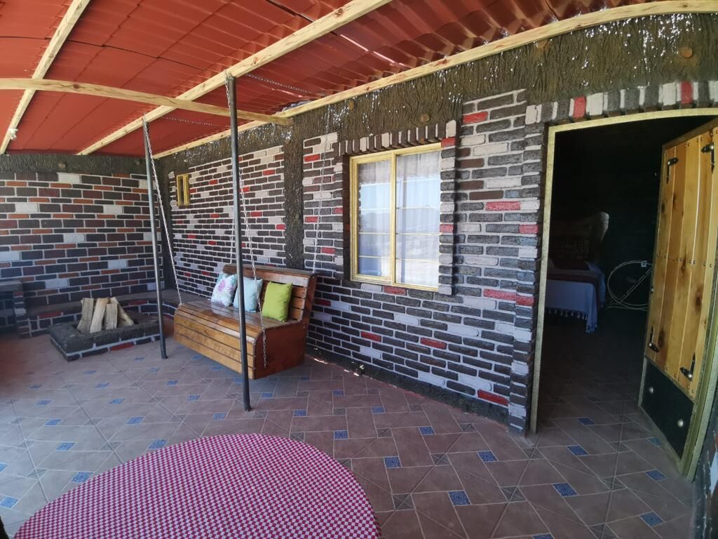 Um espaço coberto ao ar livre com parede de tijolos, um banco de madeira e um tapete com padrão vermelho e branco.