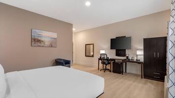 Quarto de hotel com cama, escrivaninha, cadeira, televisão, guarda-roupa e um quadro na parede.