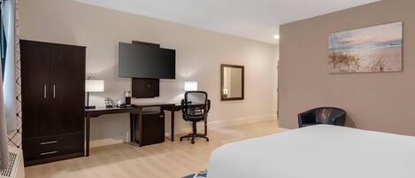 Quarto de hotel com cama, escrivaninha, cadeira, guarda-roupa, televisão e uma obra de arte na parede.
