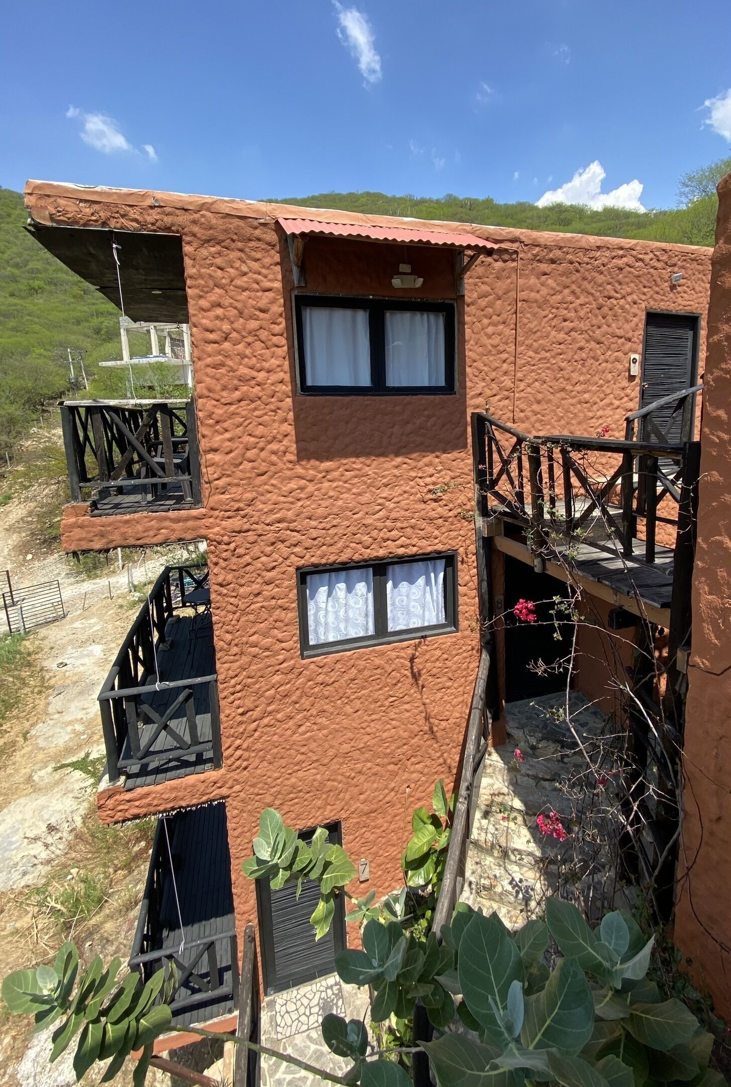 Um edifício de dois andares com fachada texturizada, varandas com guarda-corpos de madeira e janelas com cortinas.