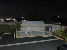 Uma área de estacionamento com um edifício murado, entrada visível e uma pequena placa.