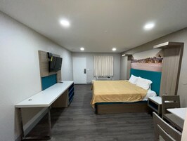 Quarto com cama, escrivaninha, televisão e janela com cortinas.
