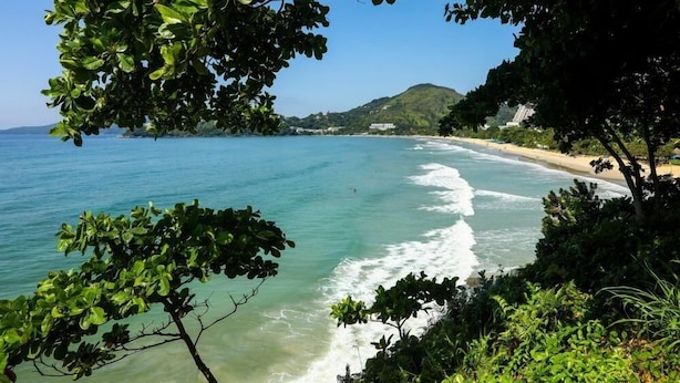 Paisagem costeira com águas azul-claras, uma praia arenosa e vegetação exuberante.