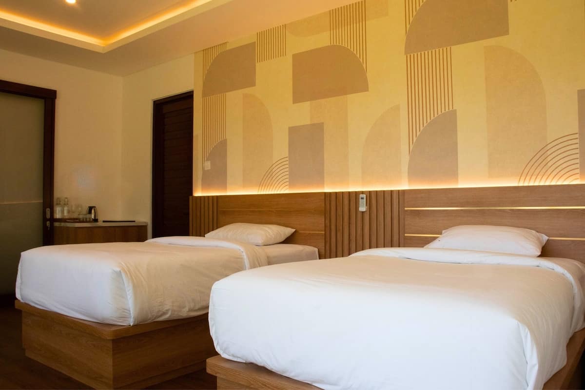 Quarto de hotel com duas camas de solteiro, cabeceiras de madeira e uma parede com padrões geométricos abstratos.
