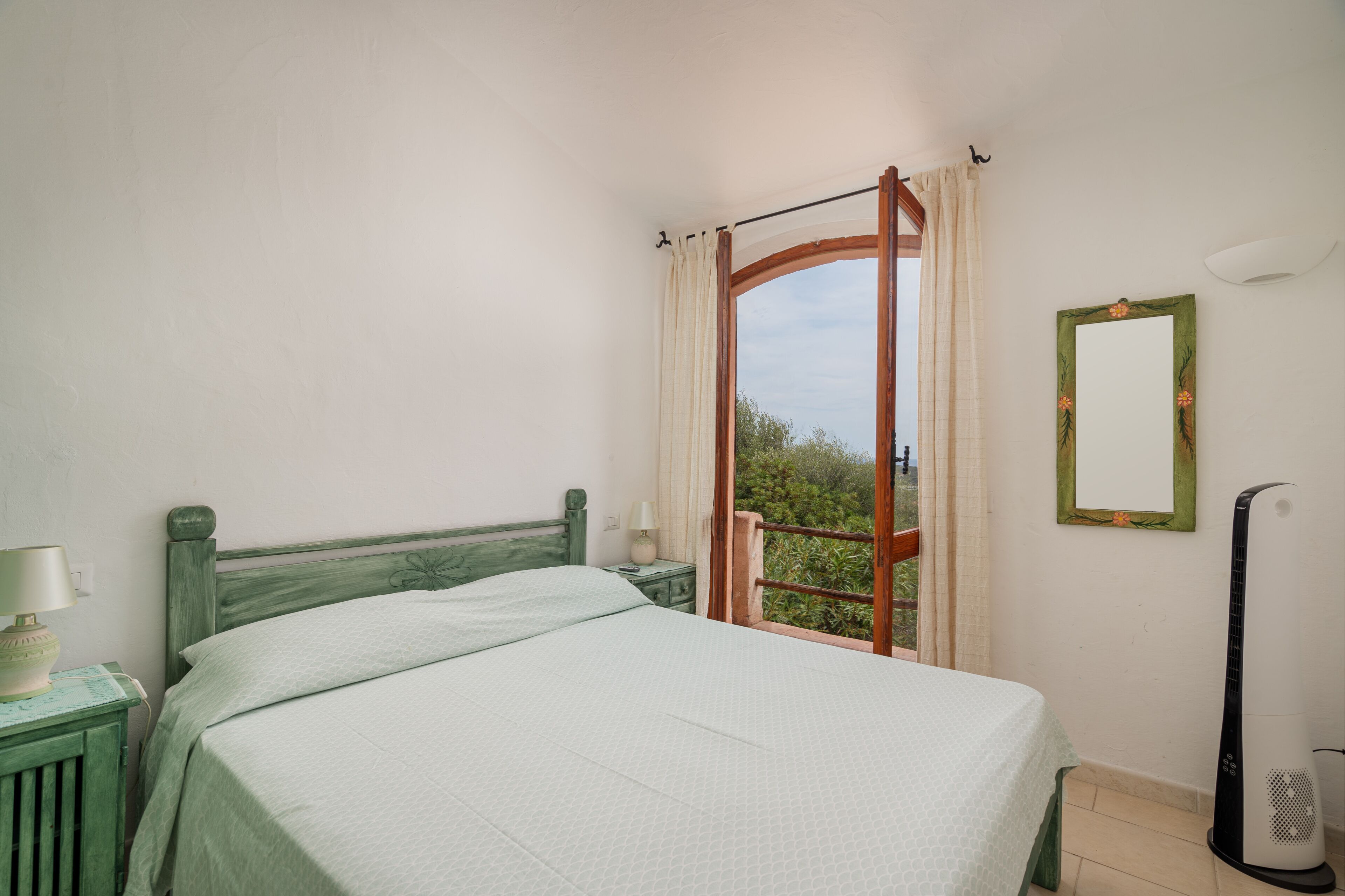 Quarto com cama, mesa de cabeceira, luminária, espelho e aquecedor.