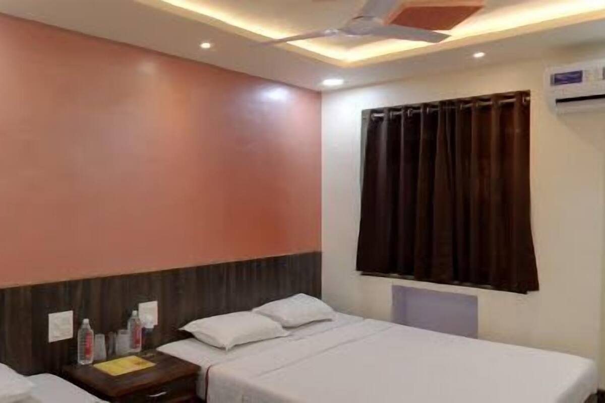Quarto de hotel com cama, mesa de cabeceira e janela com cortinas.
