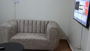 Uma sala de estar com um sofá, uma mesinha e uma TV fixada na parede.