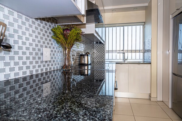 Cozinha moderna com bancada de granito, chaleira de aço inoxidável e um vaso com flores.