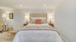 Um quarto bem arrumado com uma cama, duas luminárias de cabeceira, um criado-mudo, uma cadeira e uma pequena mesa.