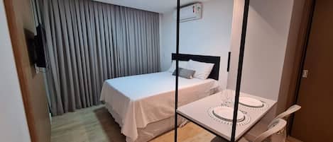 Quarto de hotel com cama, mesa de cabeceira e pequena mesa posta para dois.