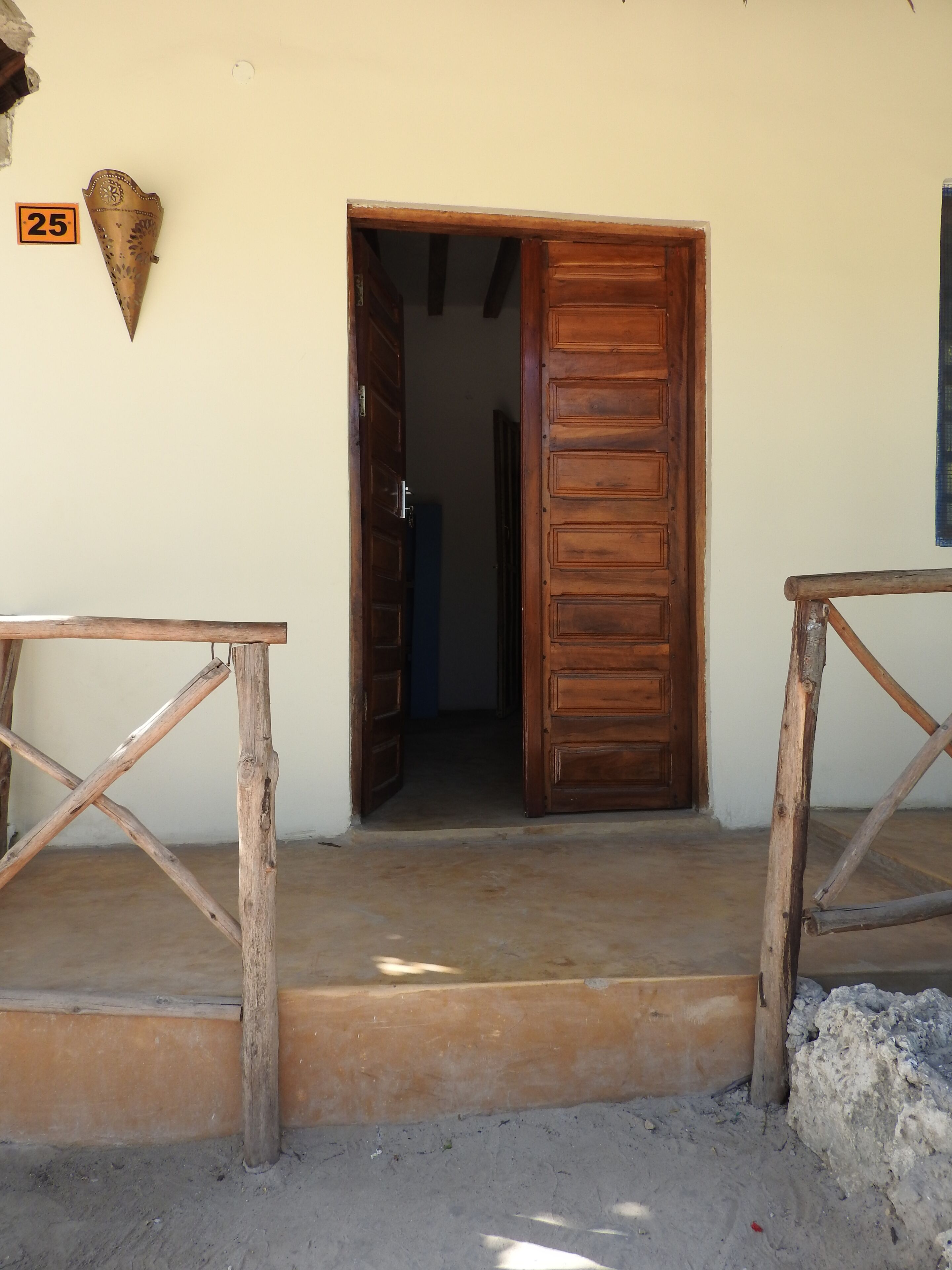 Uma porta de madeira que dá para um quarto, com uma placa com o número 25 acima.