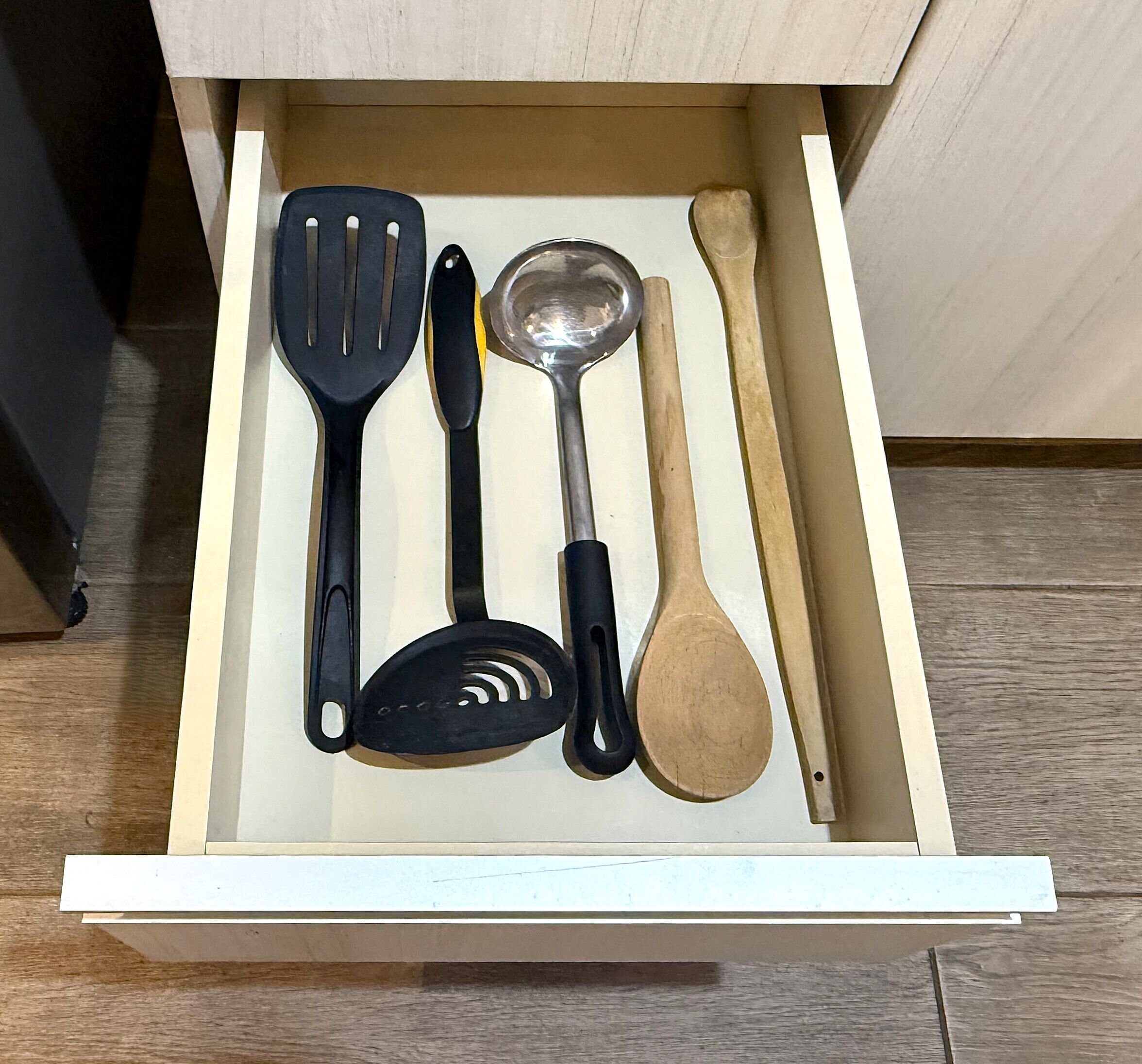 Uma gaveta com uma espátula, uma concha, uma colher de pau e um utensílio com cabo preto.