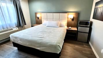 Quarto de hotel com uma cama grande, duas mesas de cabeceira, uma TV fixada na parede e ar condicionado integrado.