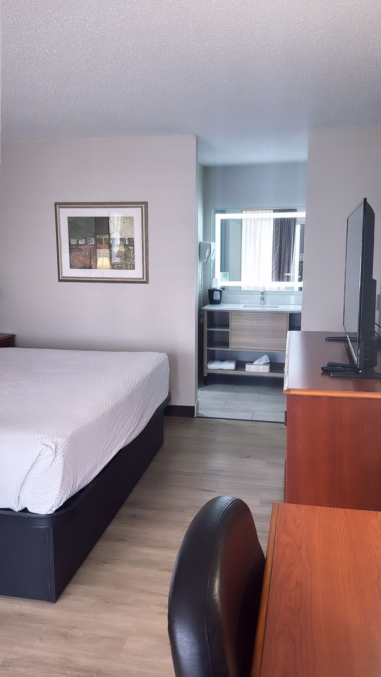 Quarto de hotel com cama, escrivaninha, cadeira, televisão e banheiro visível por uma porta aberta.