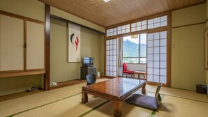 Um quarto japonês tradicional com tatames, uma mesa de madeira, portas deslizantes e uma televisão.