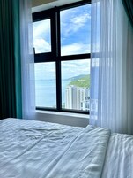 Quarto de hotel com uma grande janela que oferece vista para a paisagem urbana e colinas.