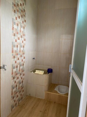 Um banheiro pequeno com parede revestida em azulejo, piso de madeira, vaso sanitário e pia com um recipiente azul.