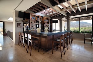 Uma área de bar com cadeiras de madeira, balcão e prateleiras com garrafas e copos.