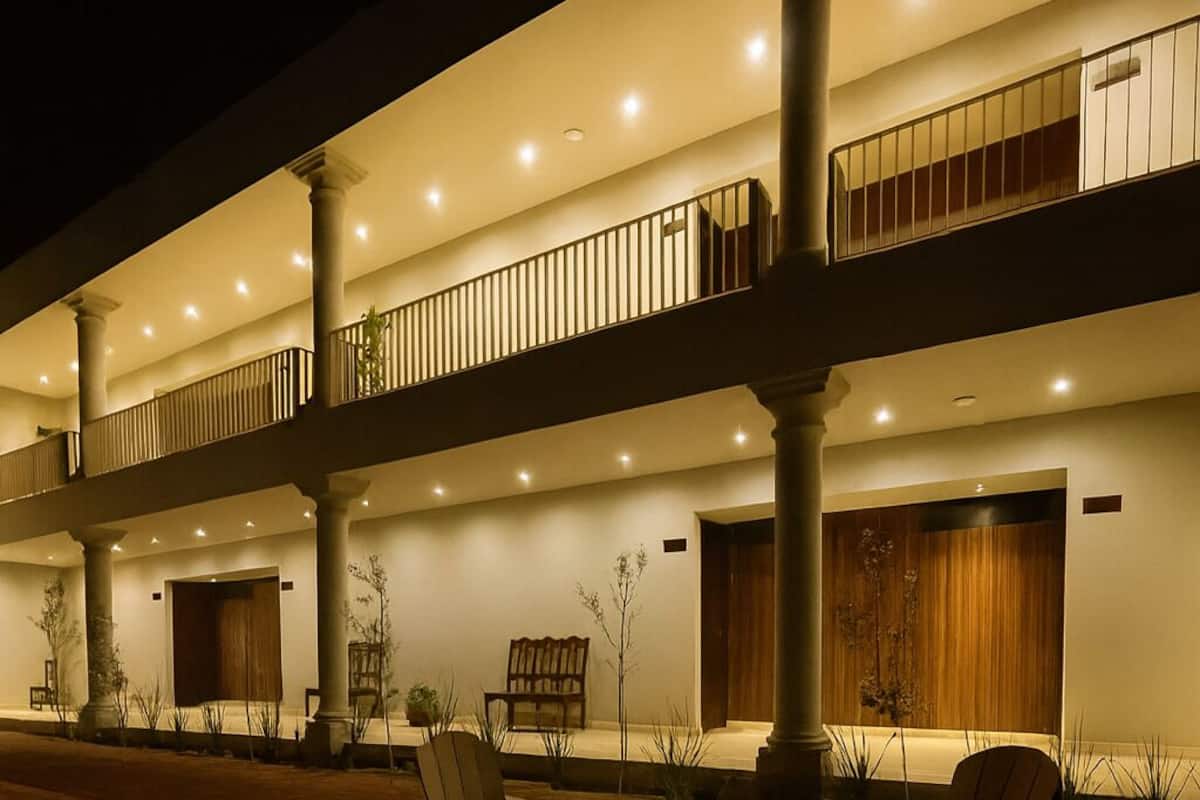 Uma área externa bem iluminada com um braseiro, cadeiras e vista para o interior do edifício.
