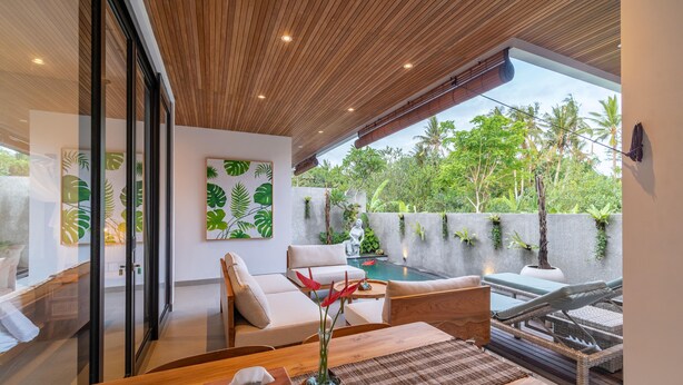 Espaço moderno em ambiente interno com teto de madeira, piscina e vista para vegetação exuberante.