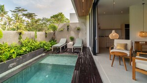 Uma área moderna de piscina ao ar livre, com espreguiçadeiras, um deck de madeira e uma cozinha visível por uma porta aberta.