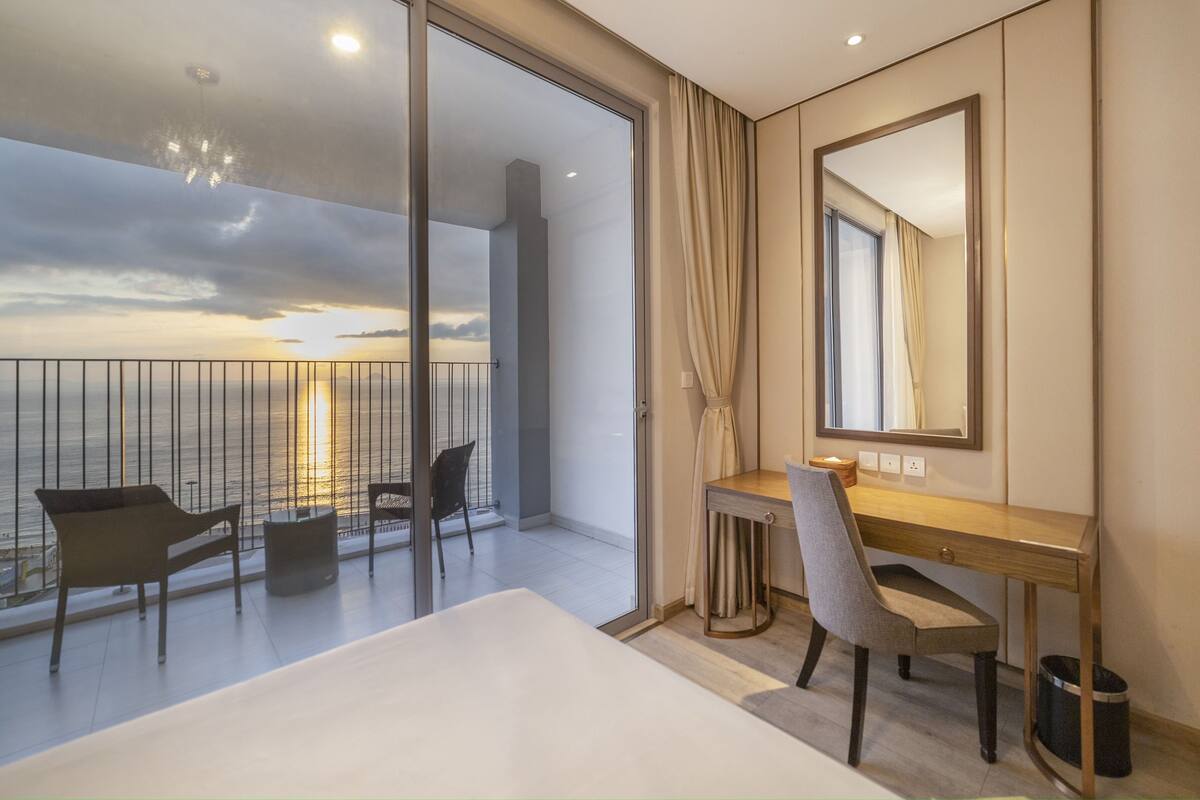 Quarto de hotel com varanda, escrivaninha, cadeira e cama.
