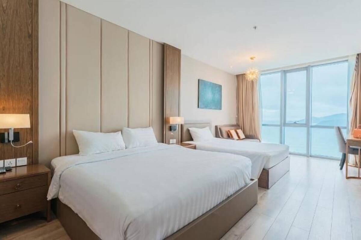 Quarto de hotel com duas camas, uma escrivaninha e uma janela grande com vista.