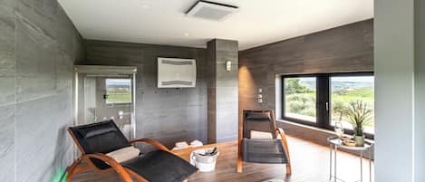 Uma sala de spa moderna com duas poltronas de descanso, uma banheira de hidromassagem e vista para o campo.