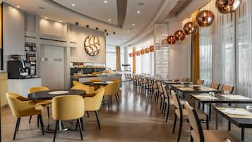 Uma área de refeições moderna com mesas redondas e cadeiras amarelas, uma máquina de café e um painel decorativo.