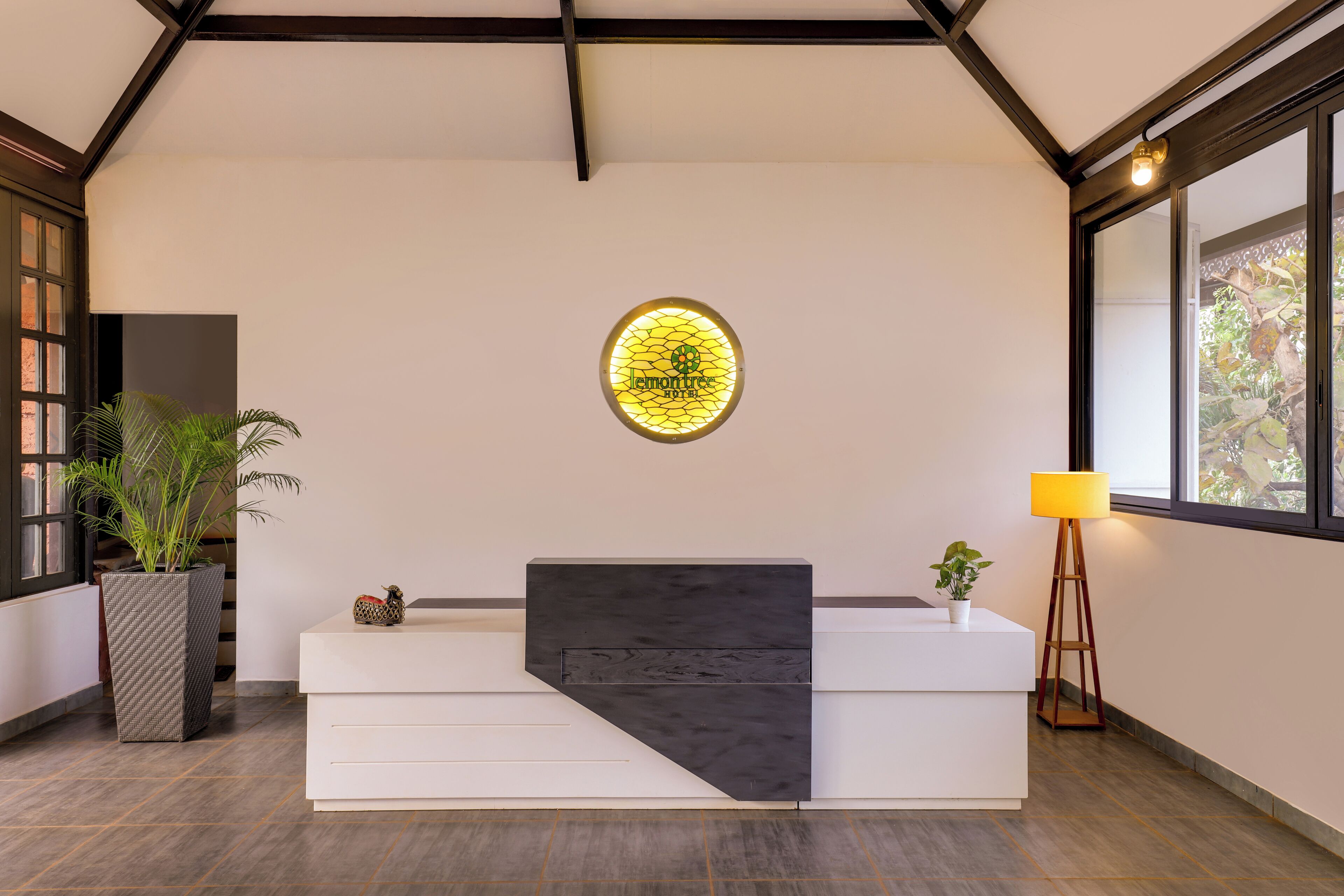 Um balcão de recepção com design moderno, um vaso de planta, uma luminária e uma placa na parede.