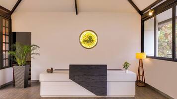 Um balcão de recepção com design moderno, um vaso de planta, uma luminária e uma placa na parede.