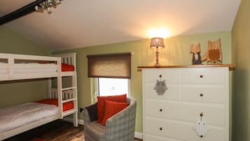 Uma cama beliche com travesseiro vermelho, uma poltrona xadrez, um penteou branco com decorações de coruja e um abajur em cima.