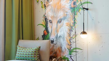 Quarto com mural de uma raposa, sofá com almofada estampada, mesa pequena e luminária suspensa.