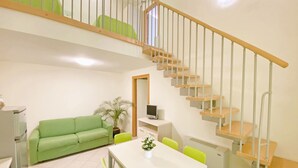 Um apartamento moderno com escada, um sofá verde, uma mesa de jantar com cadeiras e uma pequena televisão.