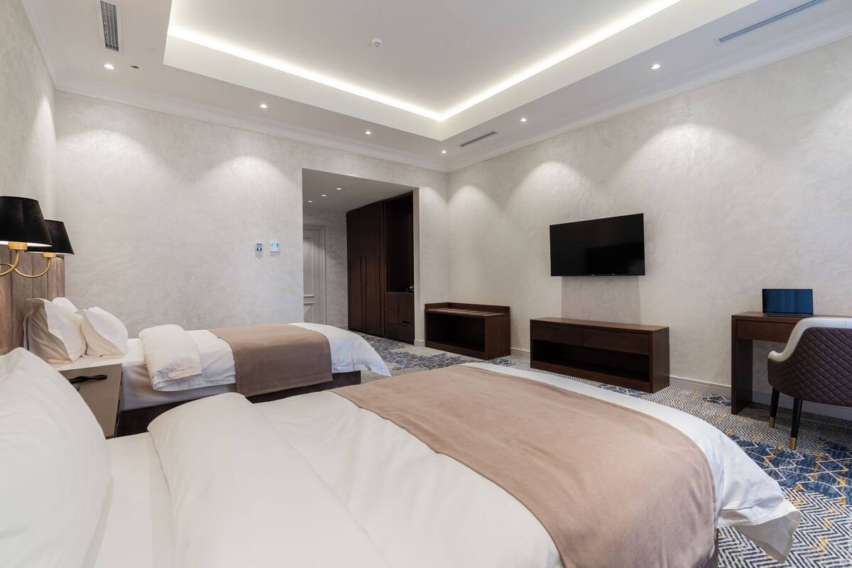 Quarto de hotel com duas camas, televisão, escrivaninha e uma cadeira.