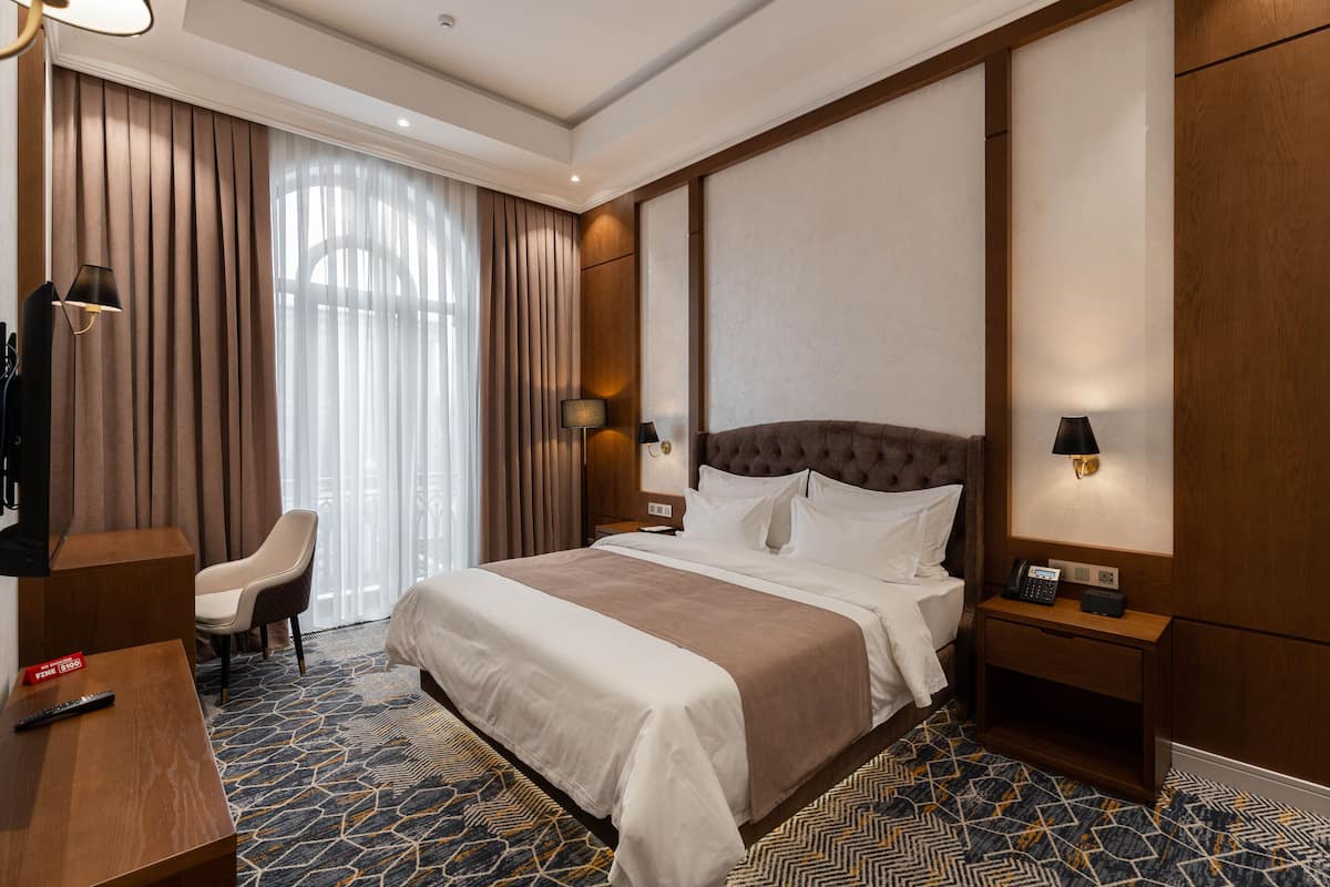 Quarto de hotel com cama grande, escrivaninha, cadeira e televisão.