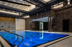 Piscina interior com vista clara da estrutura do teto e uma porta que dá para outro quarto.