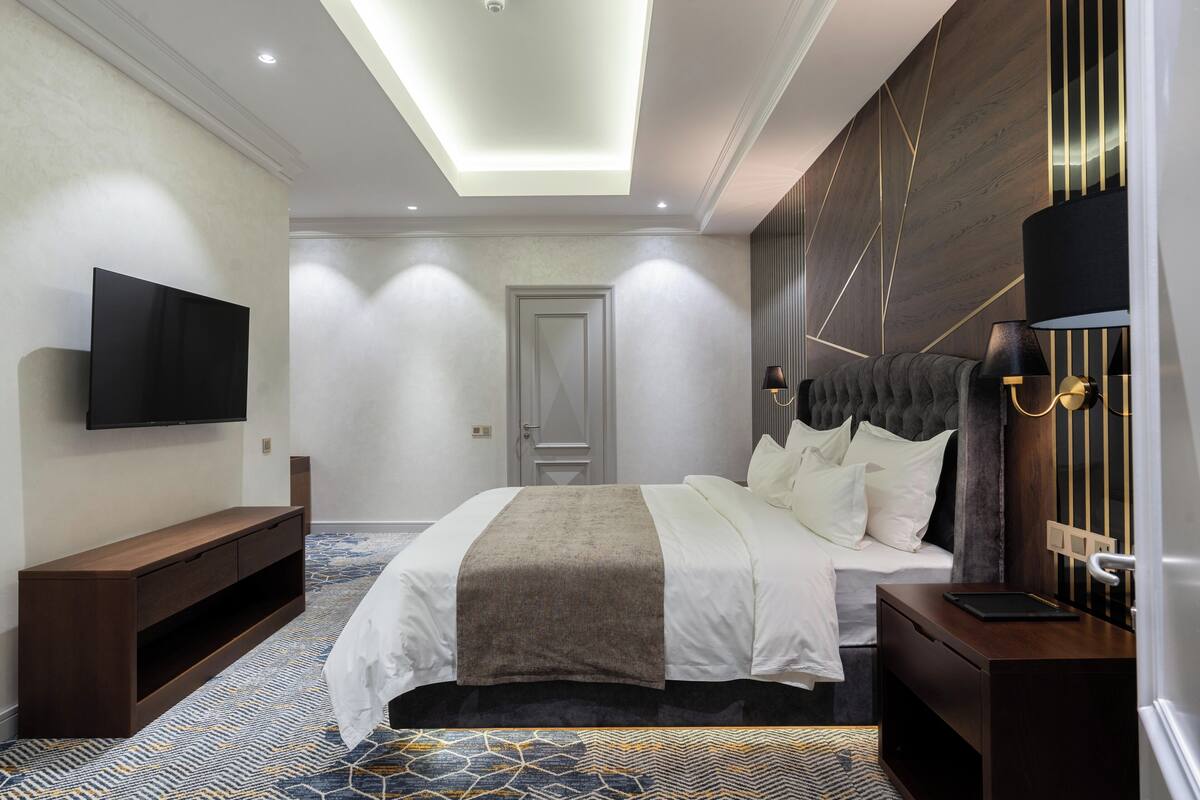 Quarto de hotel moderno com uma cama grande, televisão de tela plana, console de madeira e carpete estampado.