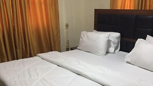 Quarto de hotel com uma cama grande, cabeceira e cortinas.