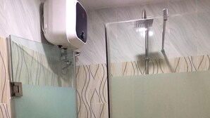 Um banheiro com porta de vidro, corrimão e dispensador de sabonete fixado na parede.