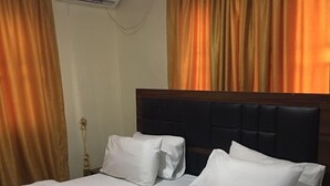 Uma cama bem arrumada com lençóis brancos, uma cabeceira de madeira e um ar condicionado fixado na parede.