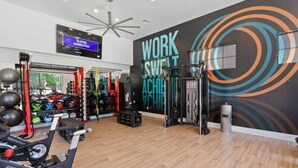Uma academia com equipamentos de exercícios, uma parede motivacional e uma tela de TV exibindo 'SUPER ARRESTED'.