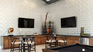 Uma mesa de bilhar em um ambiente com parede estampada, armários de madeira e duas TVs de tela plana fixadas na parede.