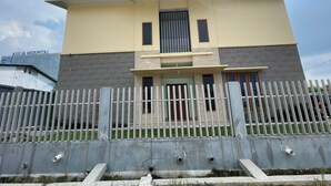 Um edifício de dois andares com telhado plano, entrada central com porta de vidro e grade de metal na frente.