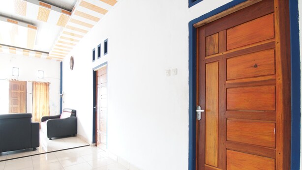 Um corredor com porta de madeira, sofá preto e piso de azulejos.
