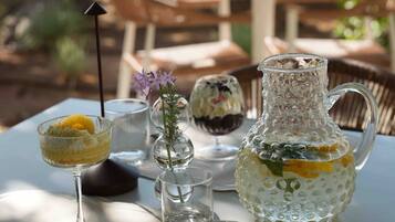 Uma mesa com um jarro, um copo, um pequeno vaso com uma flor e uma sobremesa sobre um tecido branco.