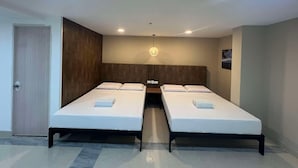 Quarto de hotel com duas camas, uma parede de destaque em madeira, uma luminária no teto e uma porta.