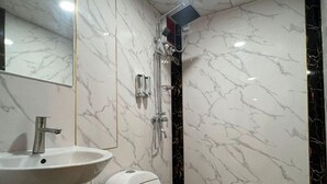 Uma casa de banho com lavatório, sanita e chuveiro brancos.